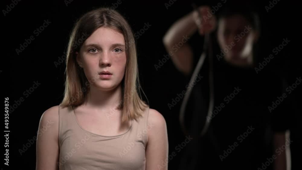 Frightened beaten teenage girl looking with fear back at blurred woman ...