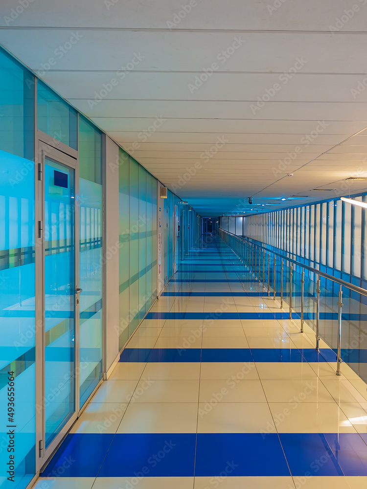 An empty long corridor with blue-and-white glass walls and doors ...