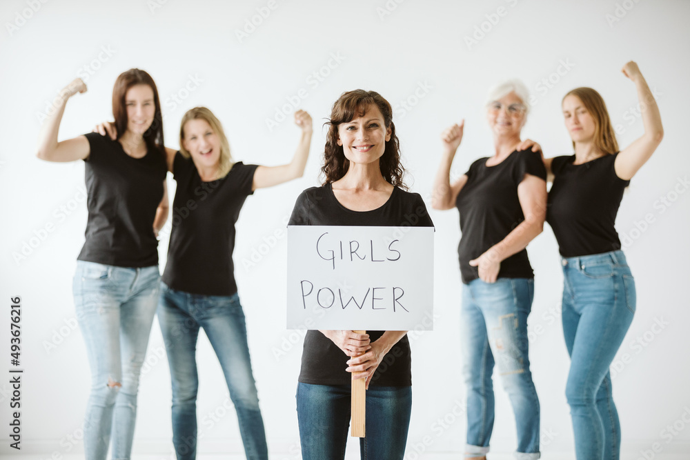 Four women dressed in jeans and black T-shirts raise their hands in a ...