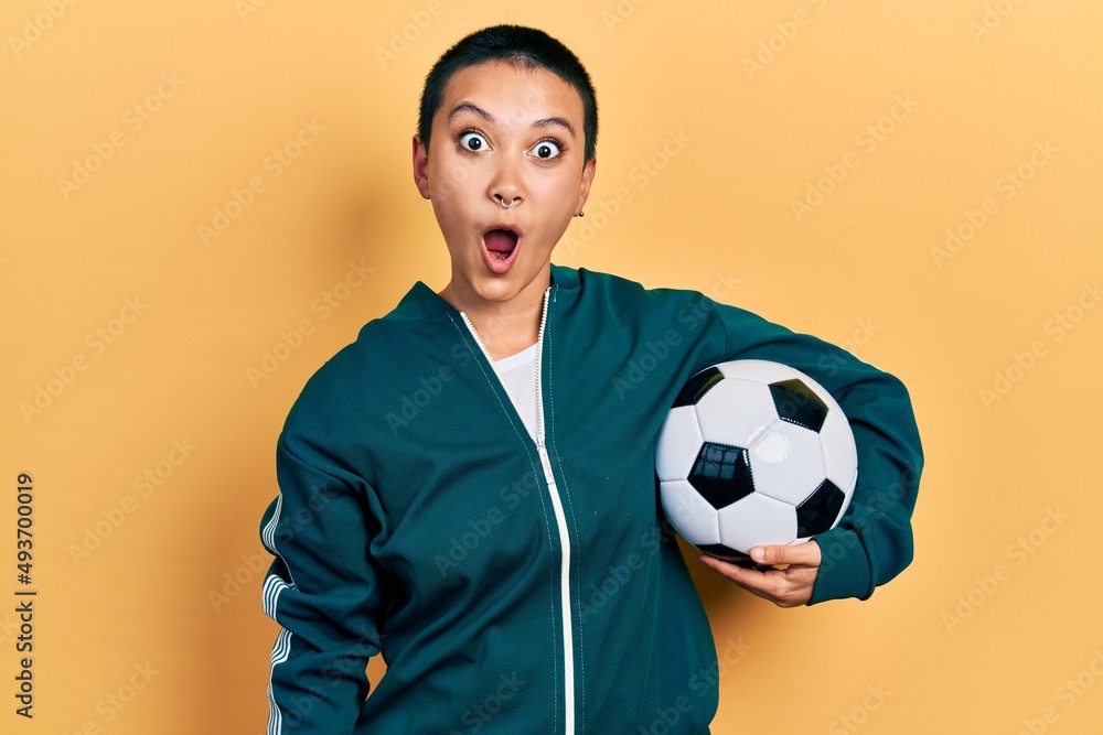 Beautiful hispanic woman with short hair holding soccer ball scared and ...