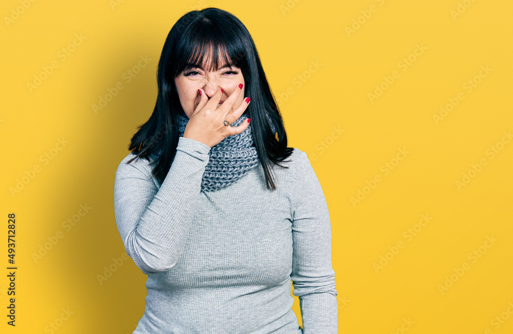 Young hispanic plus size woman wearing winter scarf smelling something ...