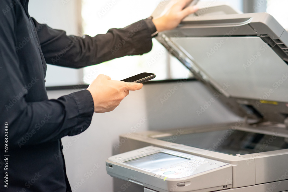 Using mobile app with photocopier. Male hand holding smartphone while ...