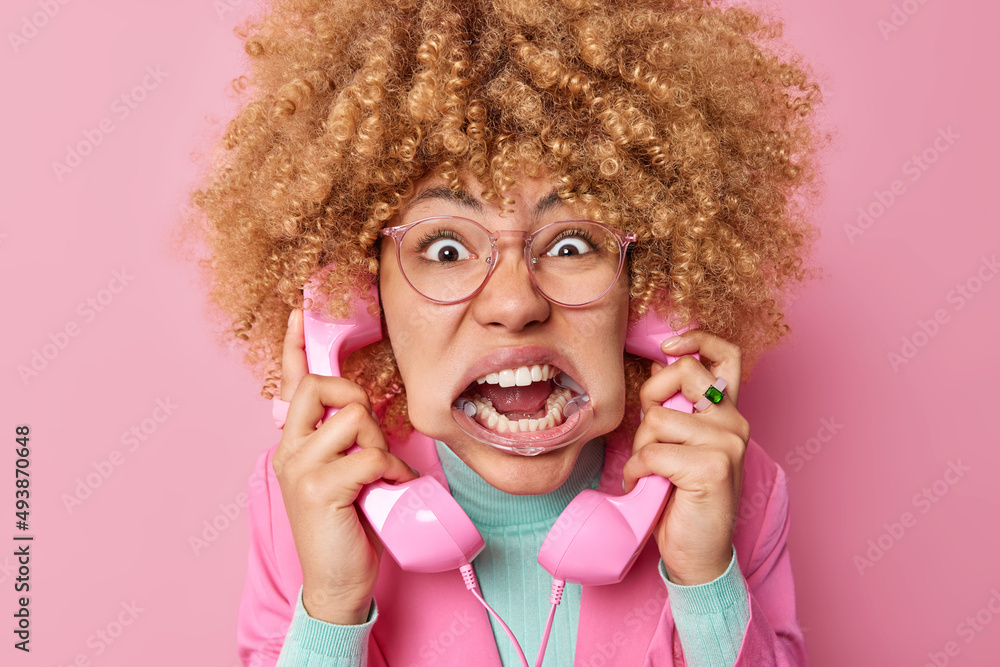 Crazy woman with curly hair holds two retro handsets near ears has ...