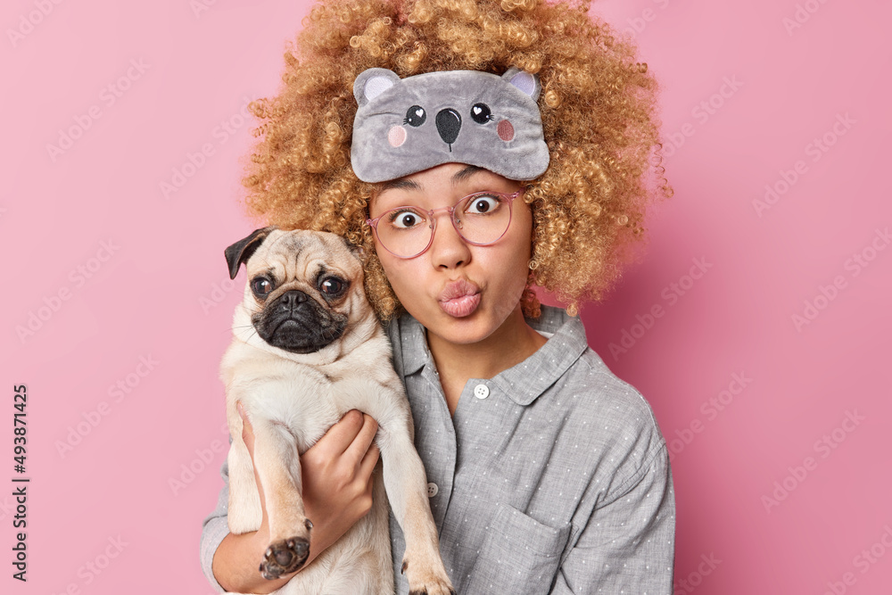 Surprised young woman with curly bushy hair keeps lips folded carries ...