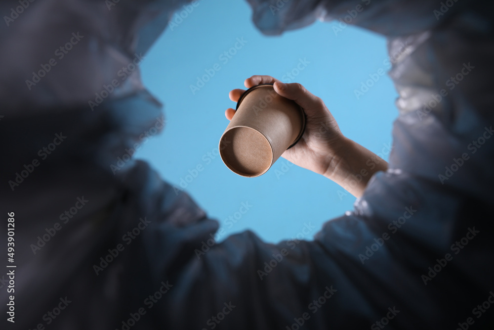 Bottom view of woman throwing paper cup into trash bin on light blue ...