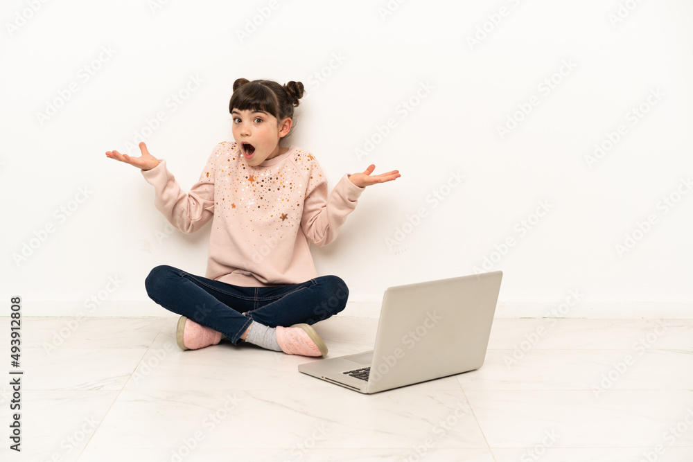 Little girl with a laptop sitting on the floor with shocked facial ...