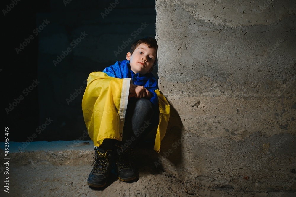 A sad Ukrainian boy wrapped in a Ukrainian flag, hiding from bombings ...
