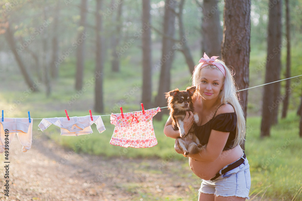 Smiling Latvian pregnant woman carrying her dog with baby laundries ...