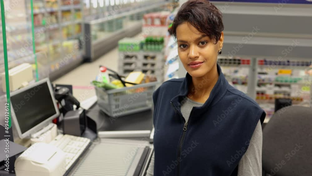 Young female cashier posing and smiling, sitting at checkout counter of ...