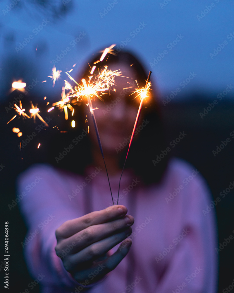 Sparklers burn in the hand of a girl in the dark blurry background ...