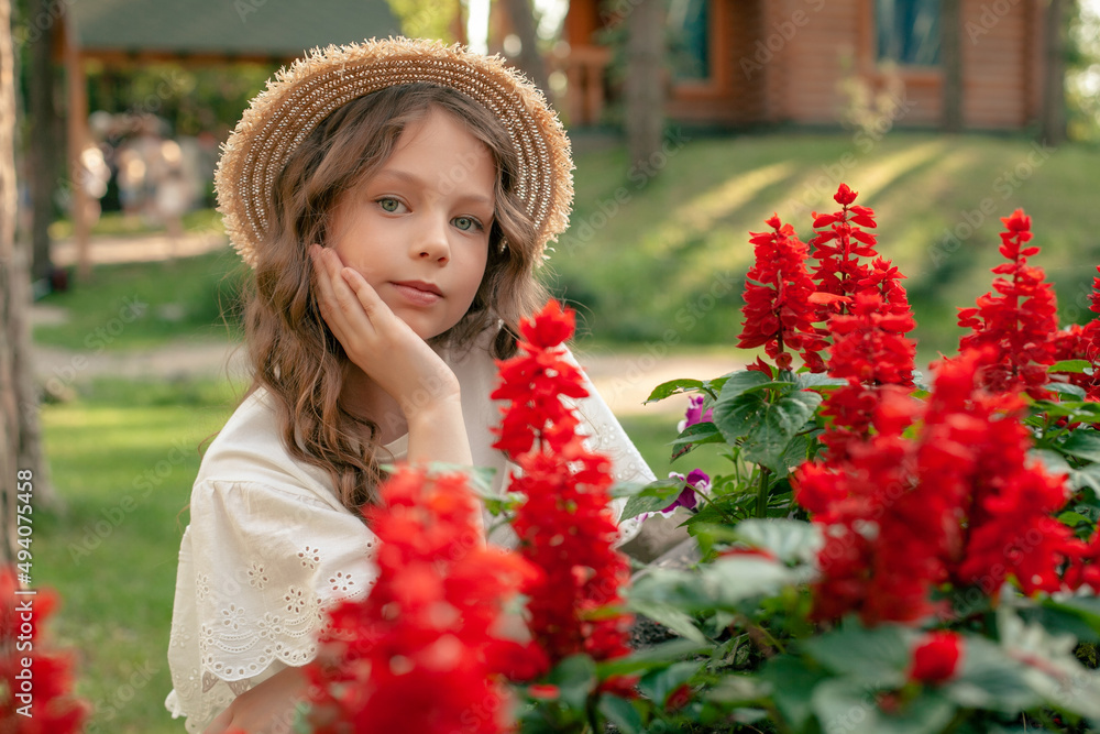 Dreamy tween girl posing near flowerbed with blooming red salvia in ...