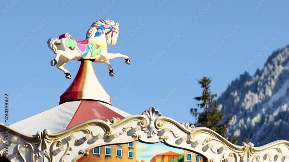 Top horse of a carousel turning with snowed white mountains at the ...