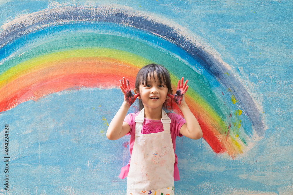 Asian Little Girl Is Painting The Colorful Rainbow And Sky On The Wall asian-little-girl-is-painting-the-colorful-rainbow-and-sky-on-the-wall