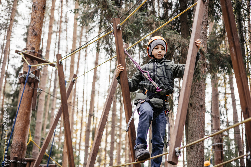 Teenager boy in safety equipment routing and climbing in adventure rope ...