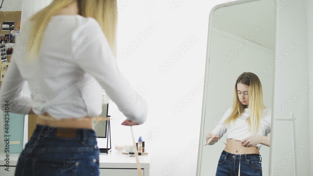 A young woman stands in front of a mirror and measures the ...