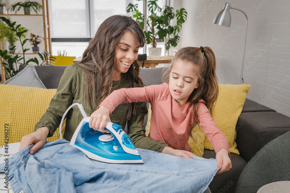 Mother teaching her cute little daughter how to iron clothes. Household ...