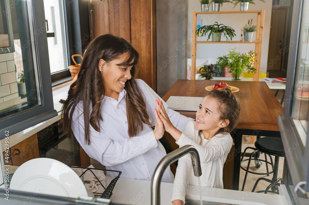 Mother and daughter washing the dishes together. Mother teaches a child ...