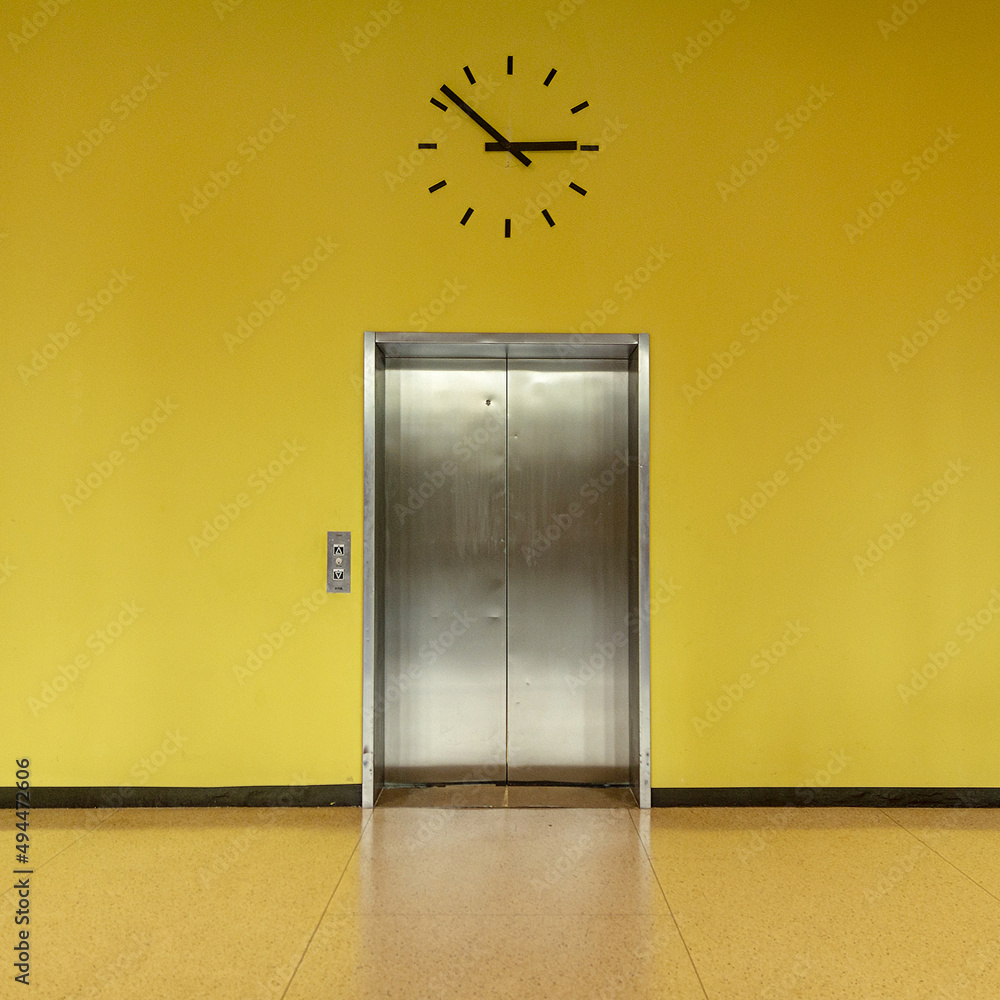 Silver elevator door with the clock above in building with yellow walls ...