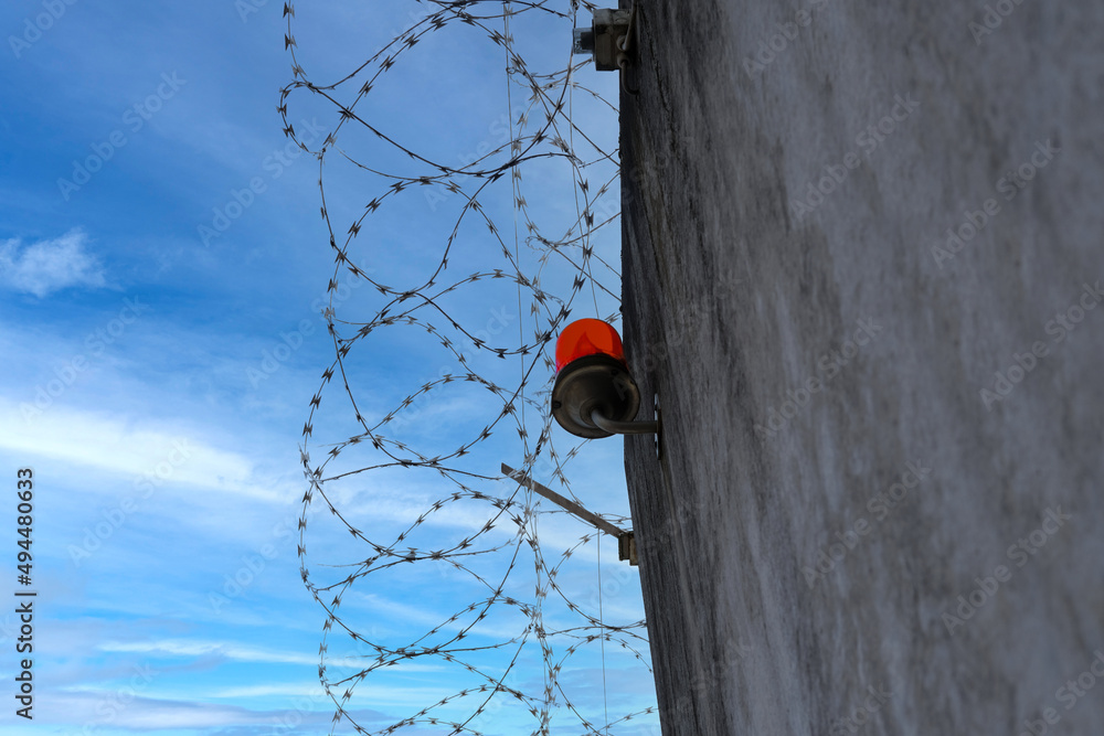many rows of barbedwire, high concrete fence, barbed wire fence on top ...