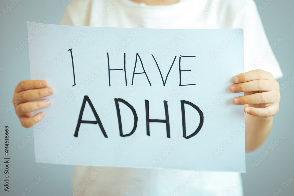 Young boy holds ADHD text written on sheet of paper. ADHD is Attention ...