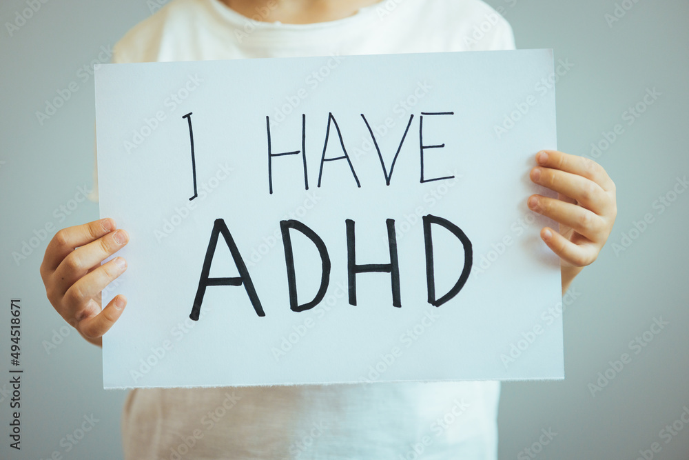 Young boy holds ADHD text written on sheet of paper. ADHD is Attention ...