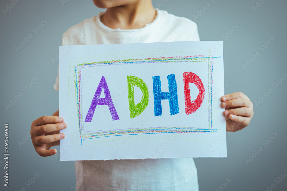 Young boy holds ADHD text written on sheet of paper. ADHD is Attention ...