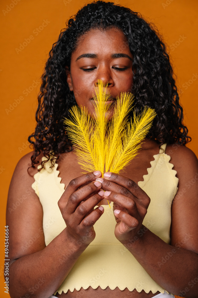 Mid waist portrait of afro woman blowing yellow soft feathers. Vertical ...