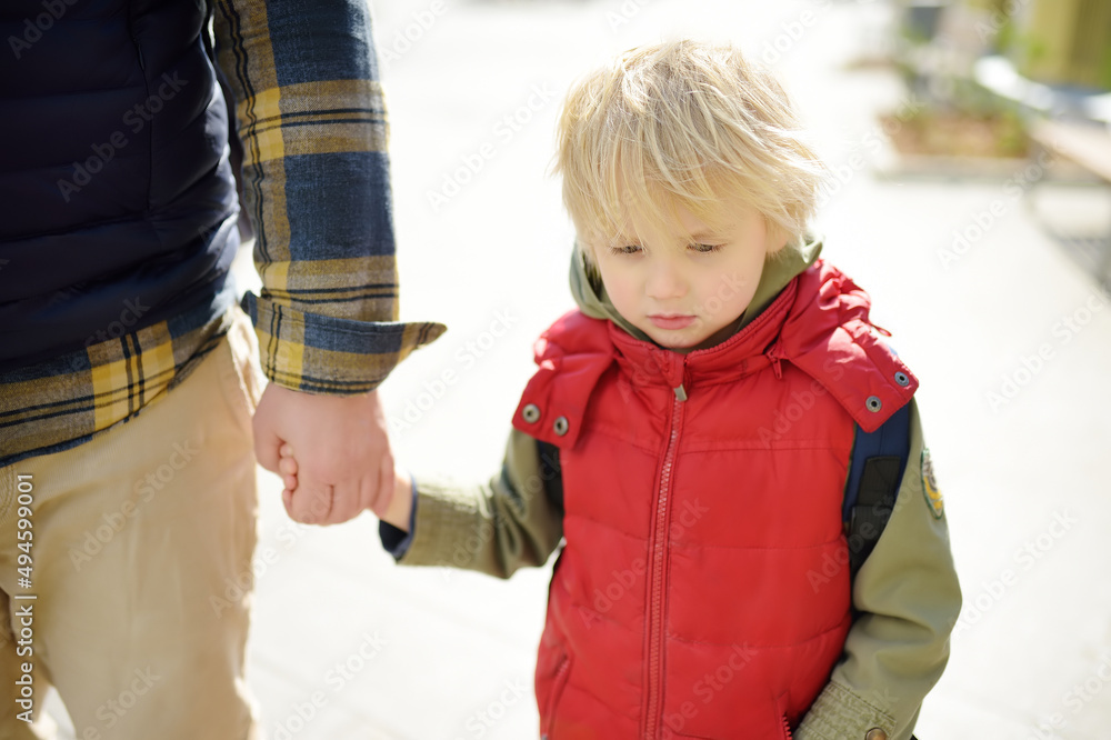Man with sad little boy are walking hand in hand along city street ...