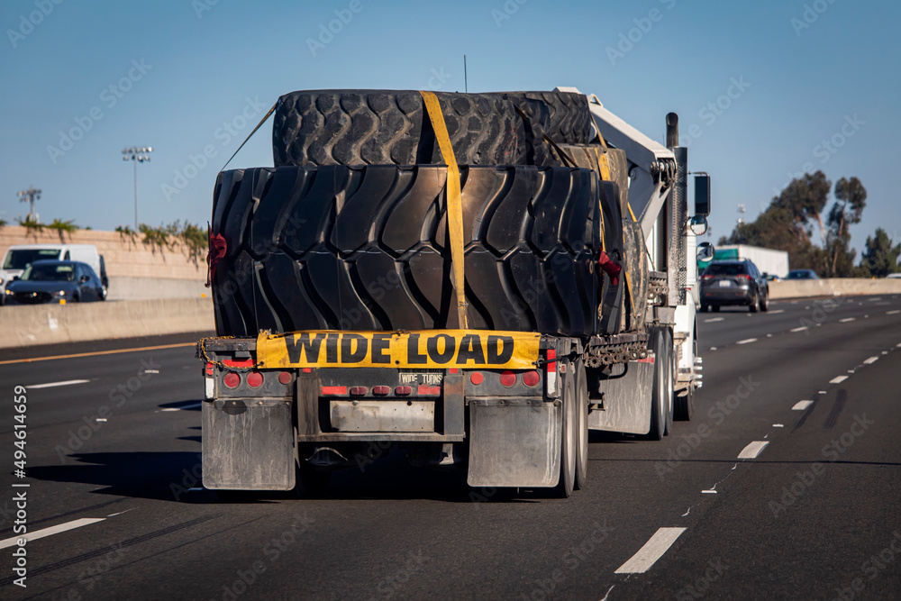 Heavy equipment tires being hauled on a flatbed trailer with a wide ...
