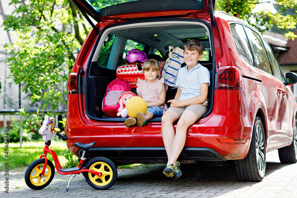Two children, school boy and preschool girl sitting in car trunk before ...