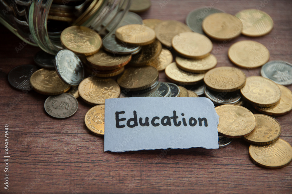 Education text on torn paper with jar, coins and wooden table ...