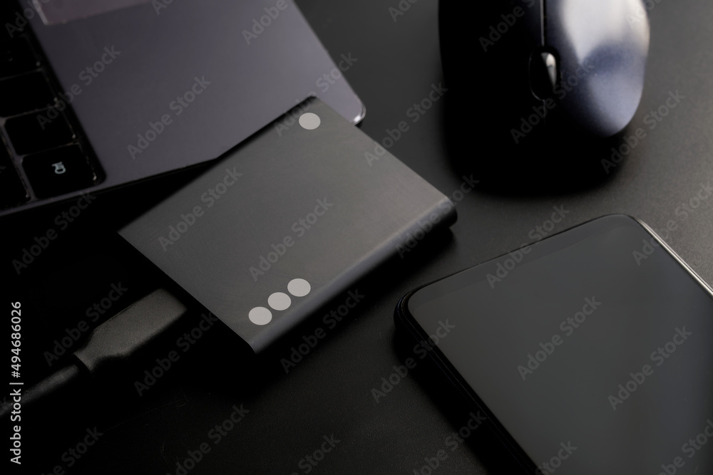 Black external portable SSD on black background next to laptop ...