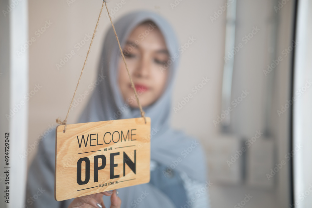 Muslim small business owner wearing hijab and turning sign to open ...