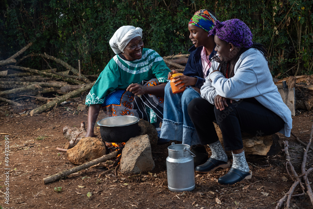 Older African Woman helping young teenage girls to prepare a pot of tea ...