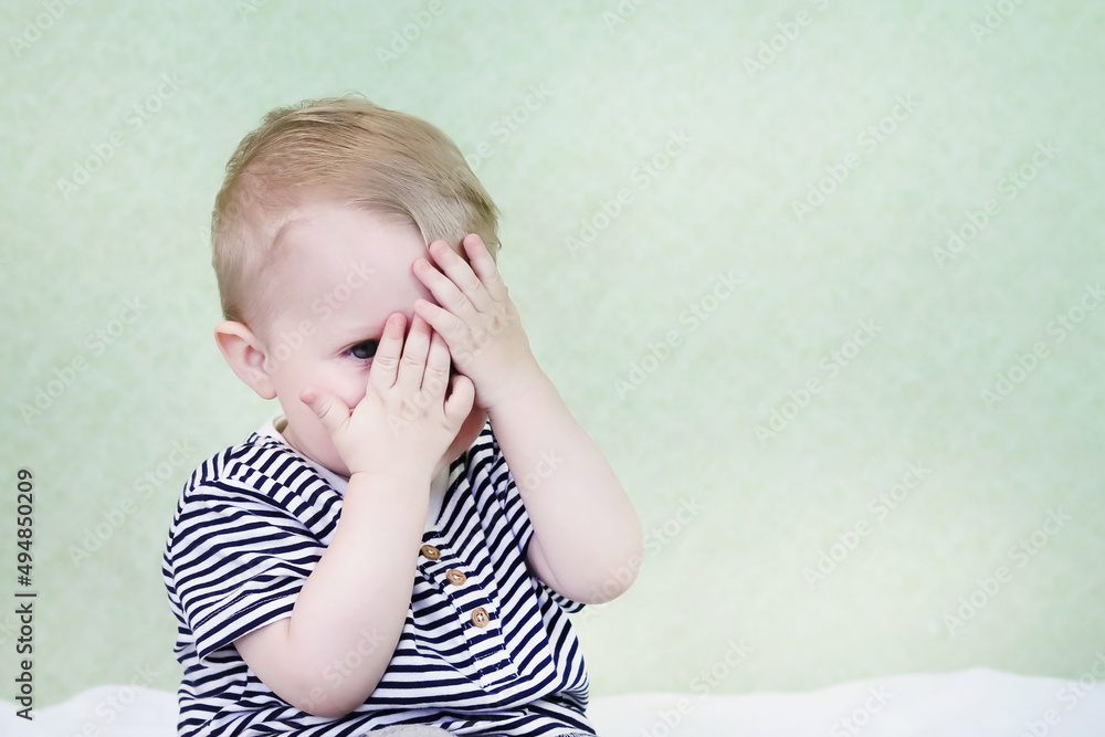 Defocused funny, happy child smiles and covers his face with his hand ...