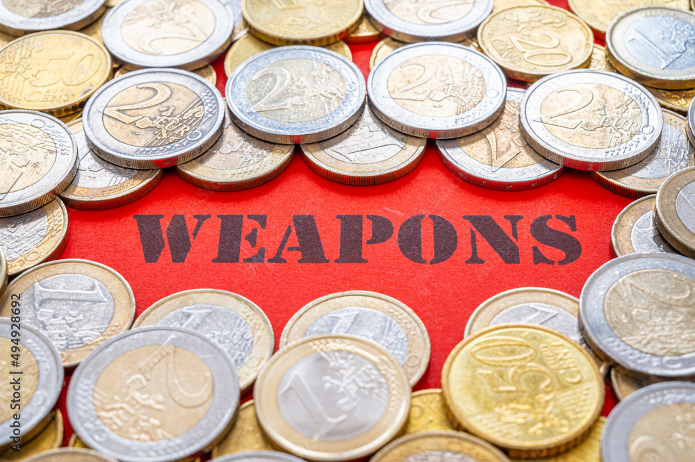Text "weapons" in black, on a red surface, and coins around it. Arms ...