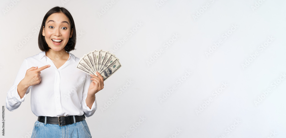 Portrait of young asian woman pointing at her money dollars, showing ...