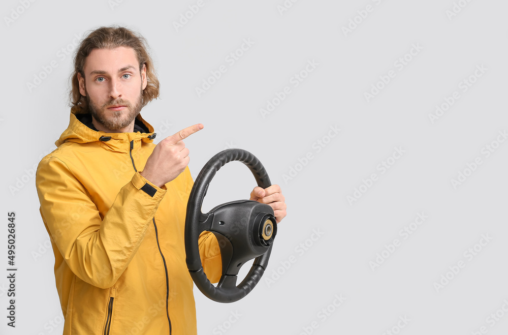 Handsome man with steering wheel pointing at something on grey ...