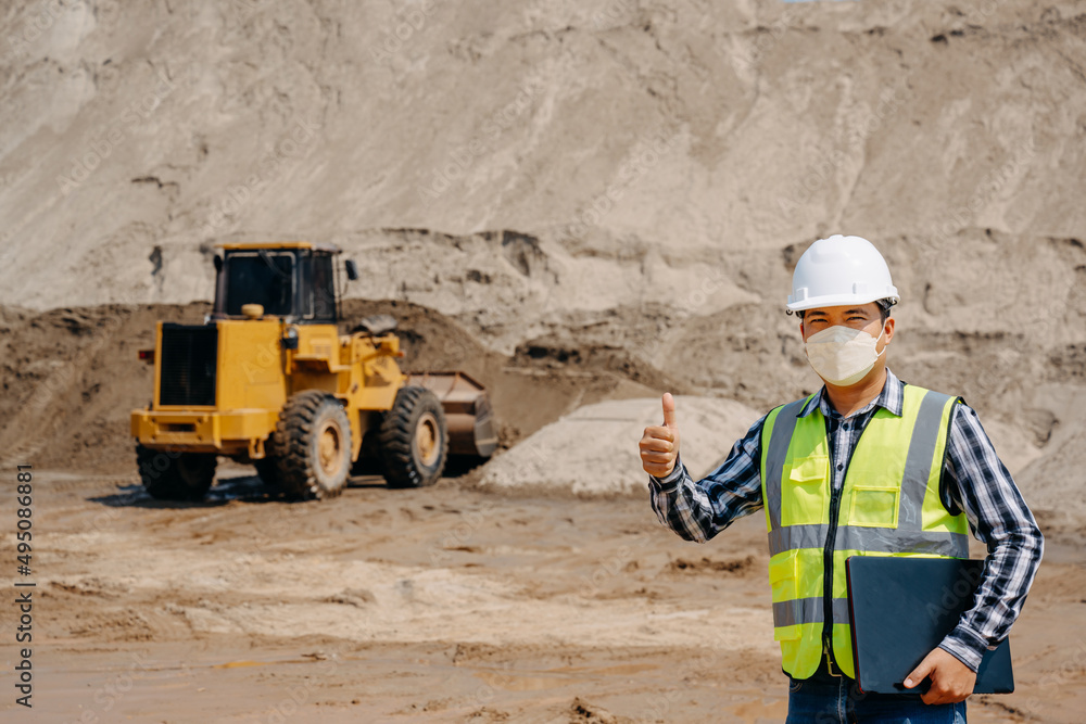 A young man civil engineer working at sand quarry inspects the ...