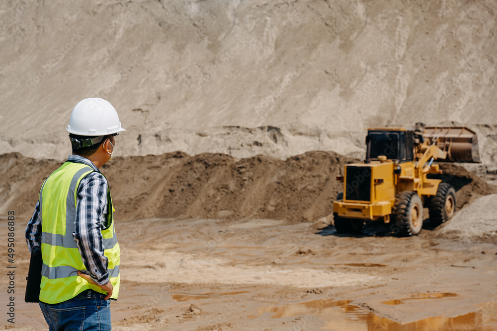 A young man civil engineer working at sand quarry inspects the ...