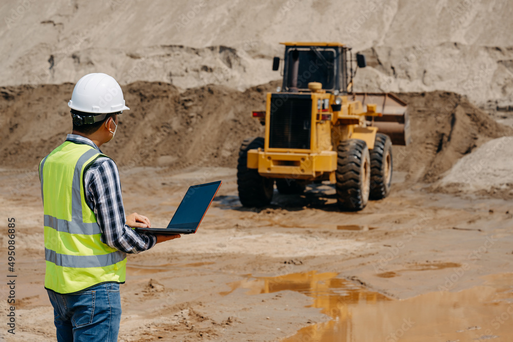 A young man civil engineer working at sand quarry inspects the ...