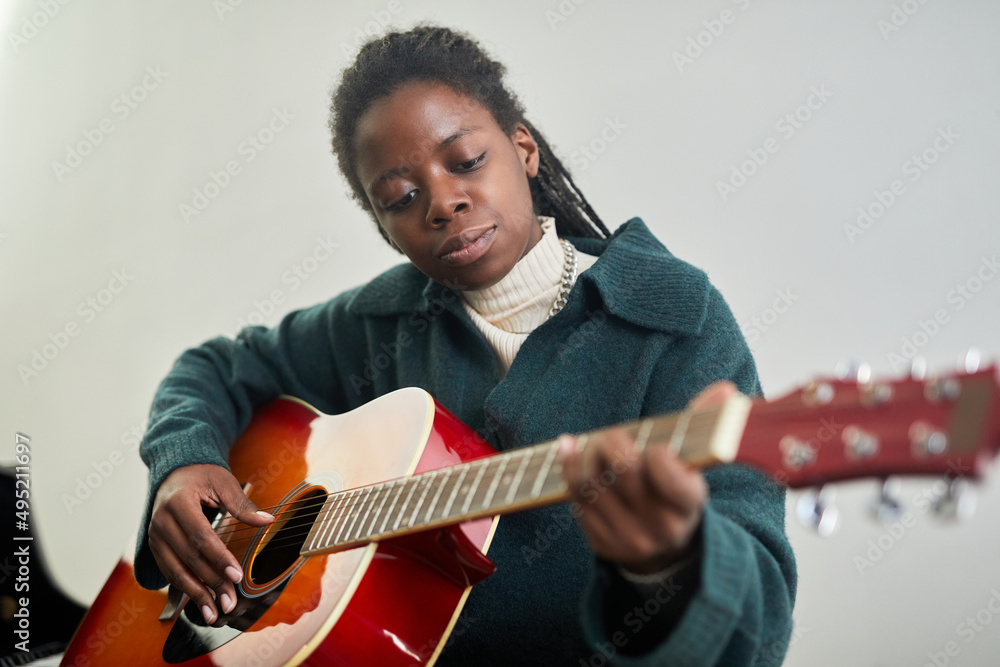 African teenage girl concentrating on her play on the guitar, she ...