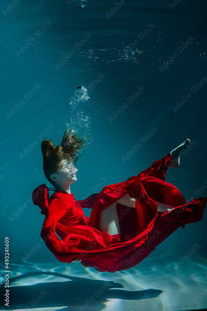Attractive red-haired young woman swims beautifully underwater in a red ...