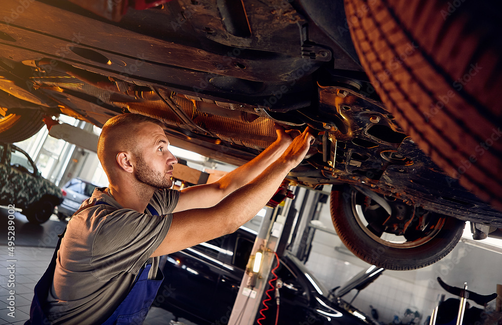 Auto mechanic checking running gear of automobile on service station ...