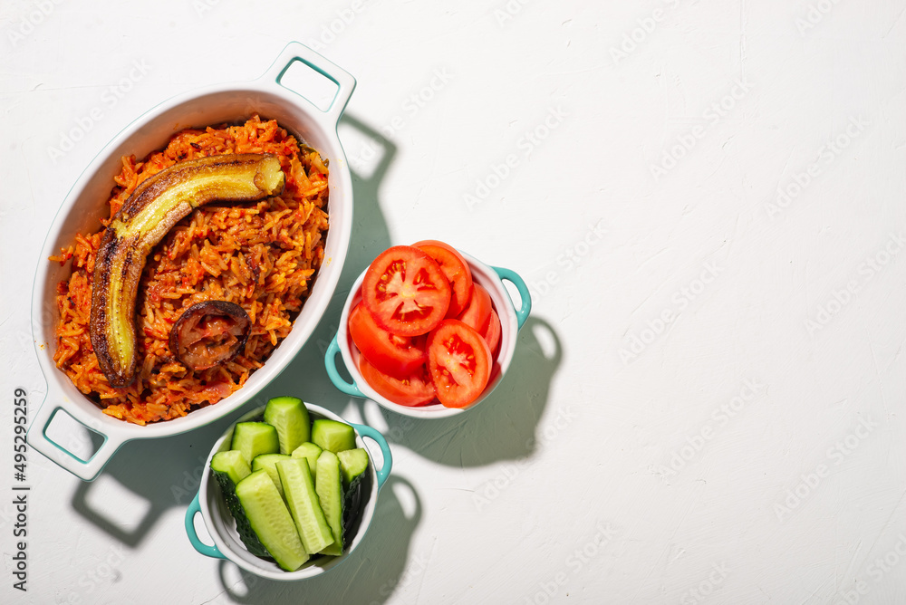 Jollof rice with fried banana. Fresh vegetables - tomato and cucumber ...