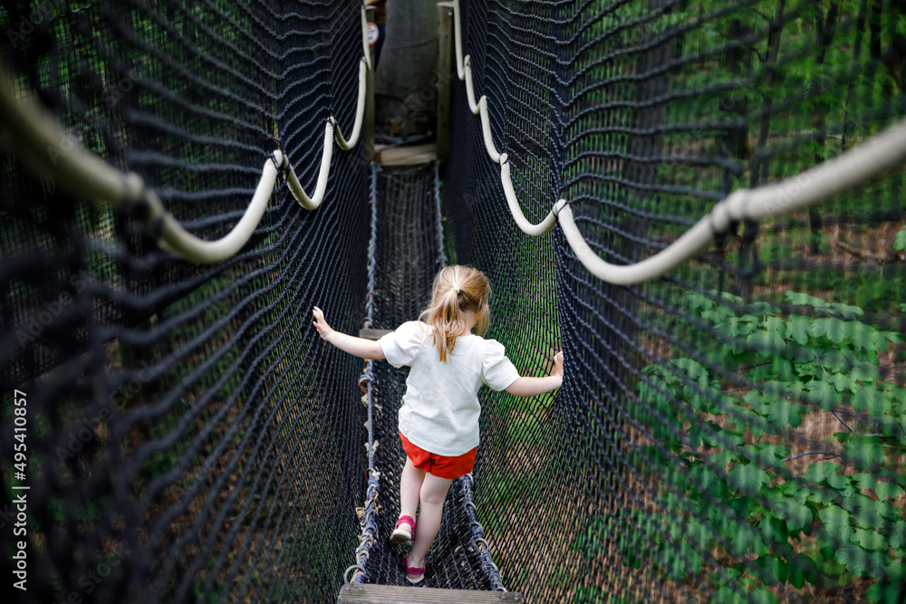 Cute little preschool girl walking on high tree-canopy trail with ...