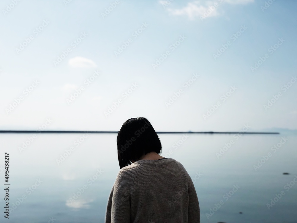 Back view of sad woman standing by seashore Stock Photo | Adobe Stock