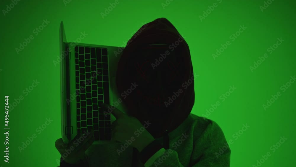 Mysterious hooded person with LED XX mask holding laptop, neon green ...
