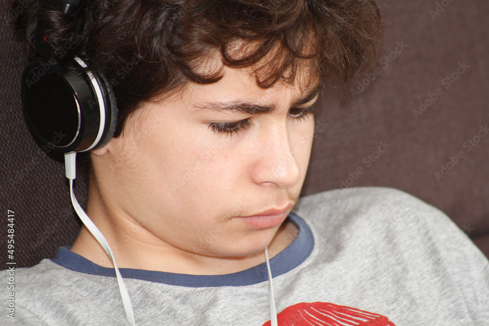 Earnest teenage boy working from a computer with headphones in his ears ...