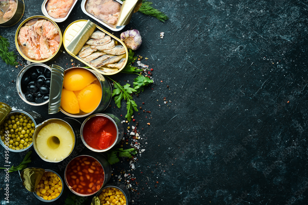Canned vegetables, beans, fish and fruits in tin cans on black stone ...